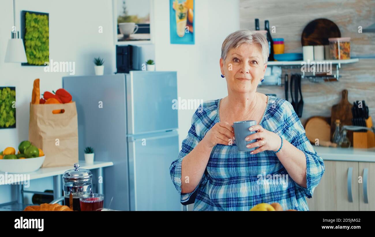 Grandmother taking cup of hot coffee for counter in kitchen during ...