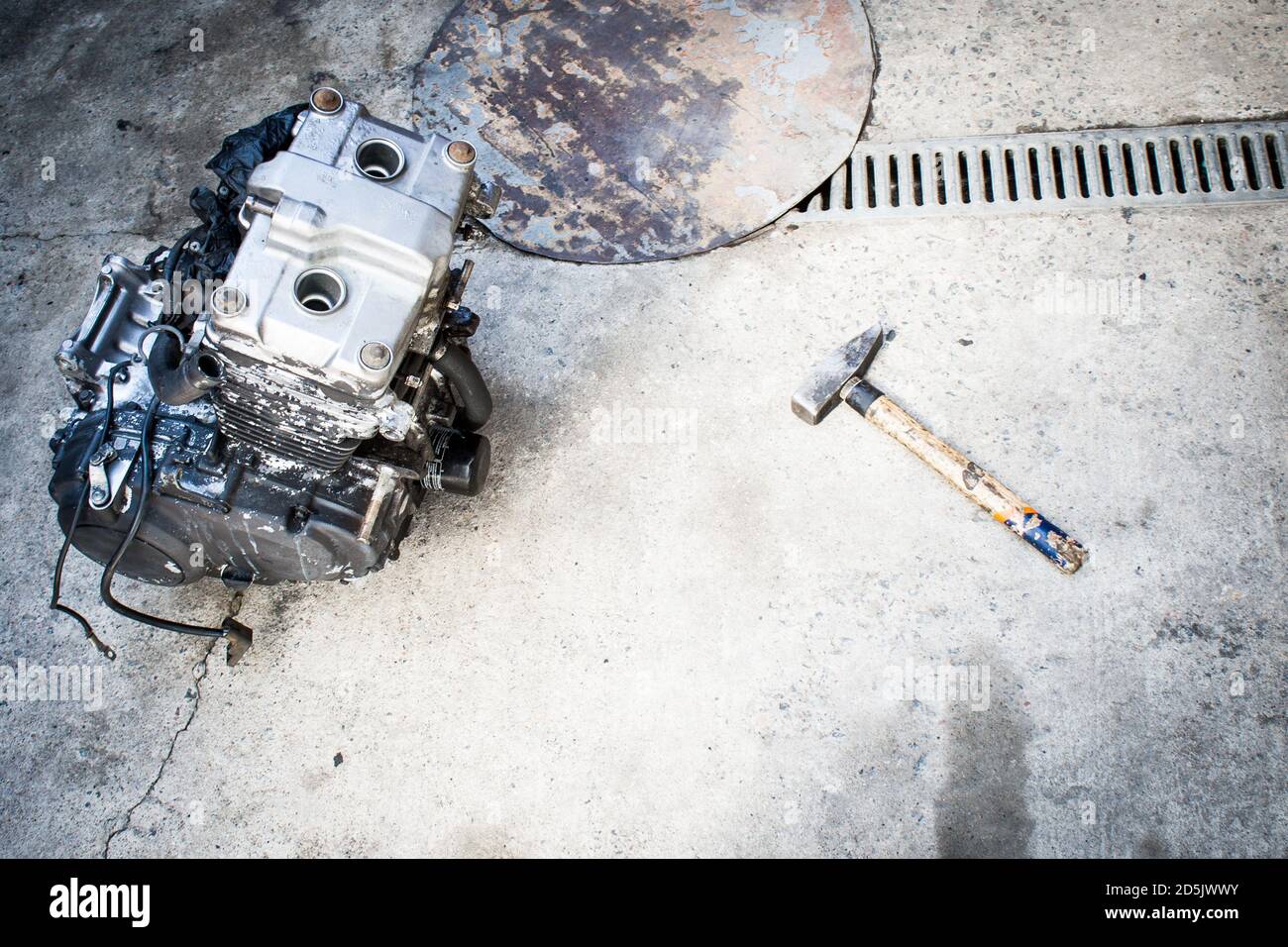 Old motor from a motorcycle with a hammer on concrete in a workshop ...