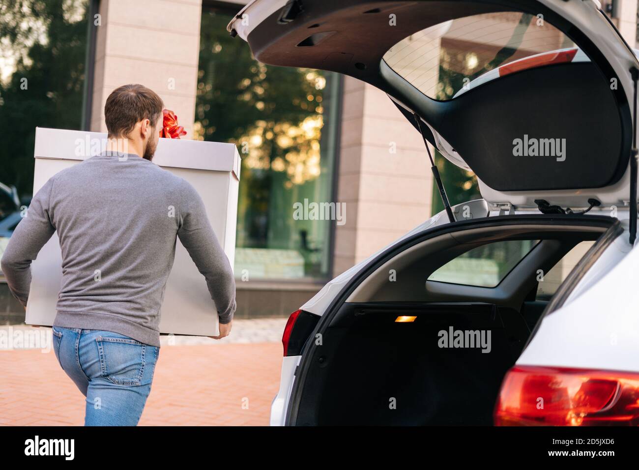 Back view of delivery man takes out large festive white box with ...