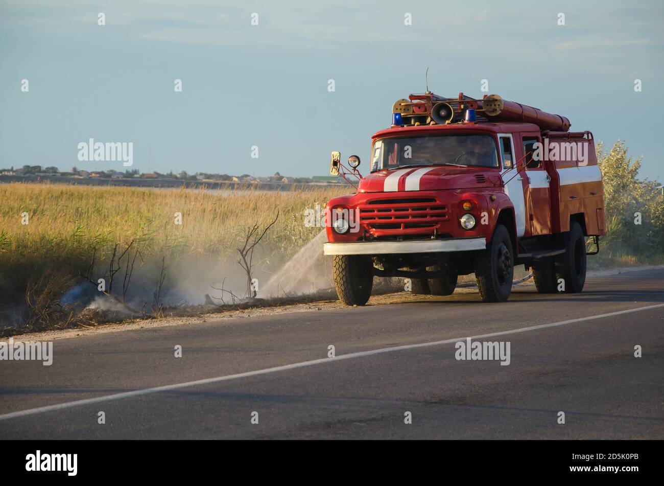 An old firetruck extinguishes a fire near the road. The grass is ...