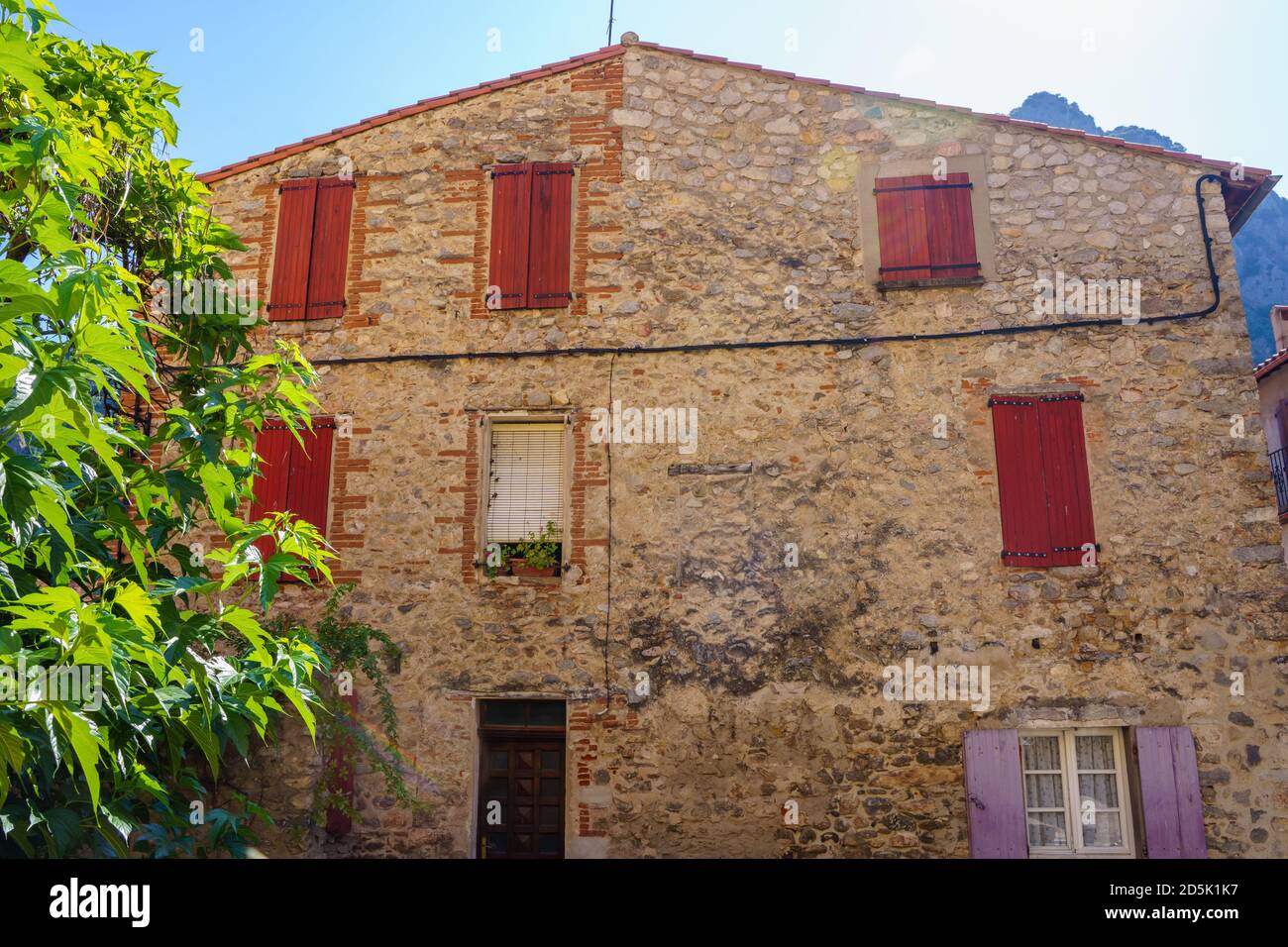 Facade of a rural stone house with colored window frames on a sunny day ...