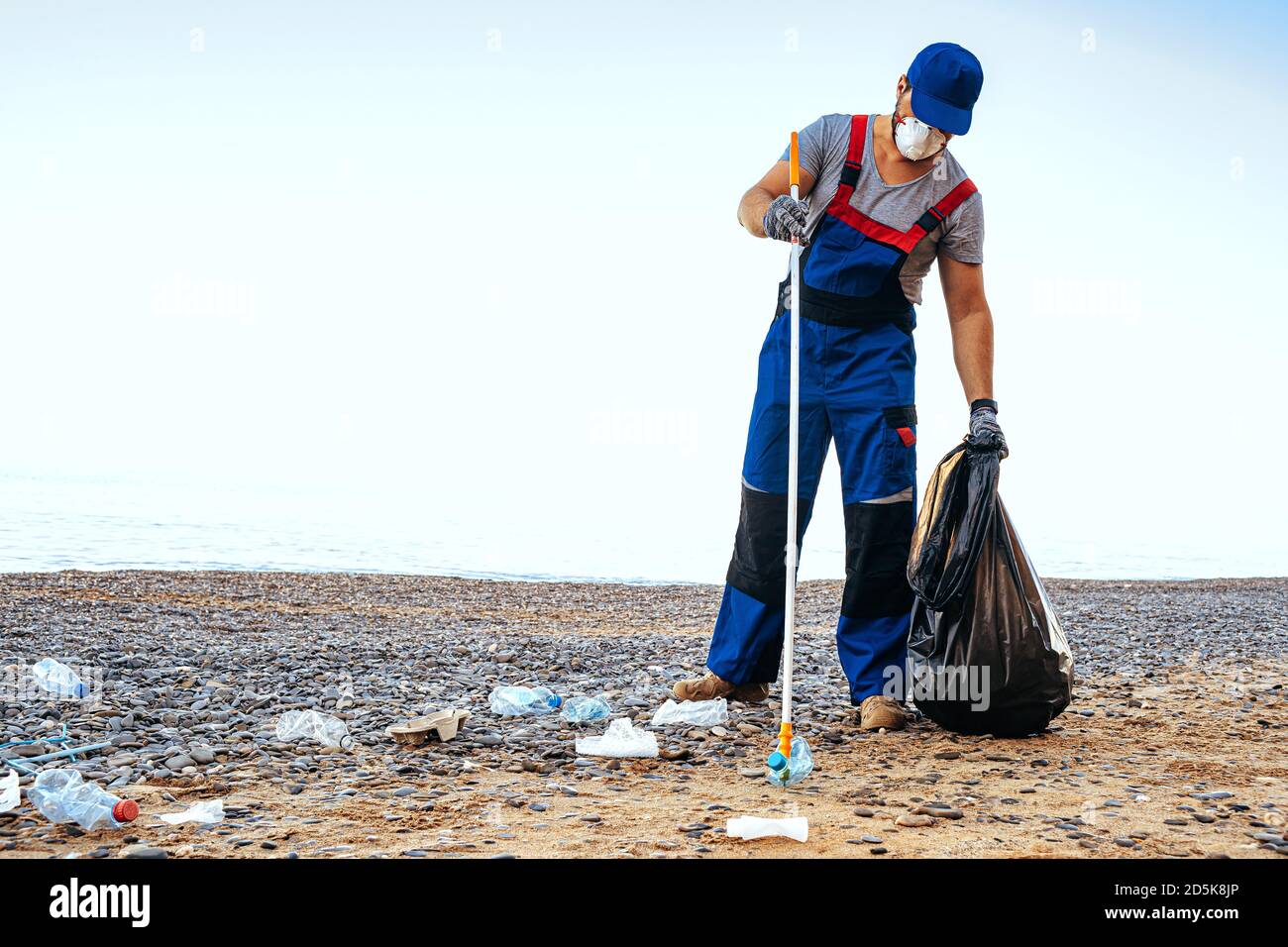 Man volunteer collecting garbage on the beach with a reach extender ...