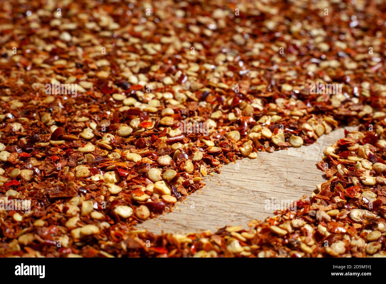 Chili flakes on wooden surface background with a chili shape on the ...