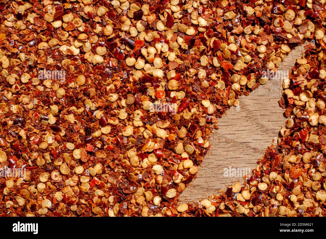 Chili flakes on wooden surface background with a chili shape on the ...
