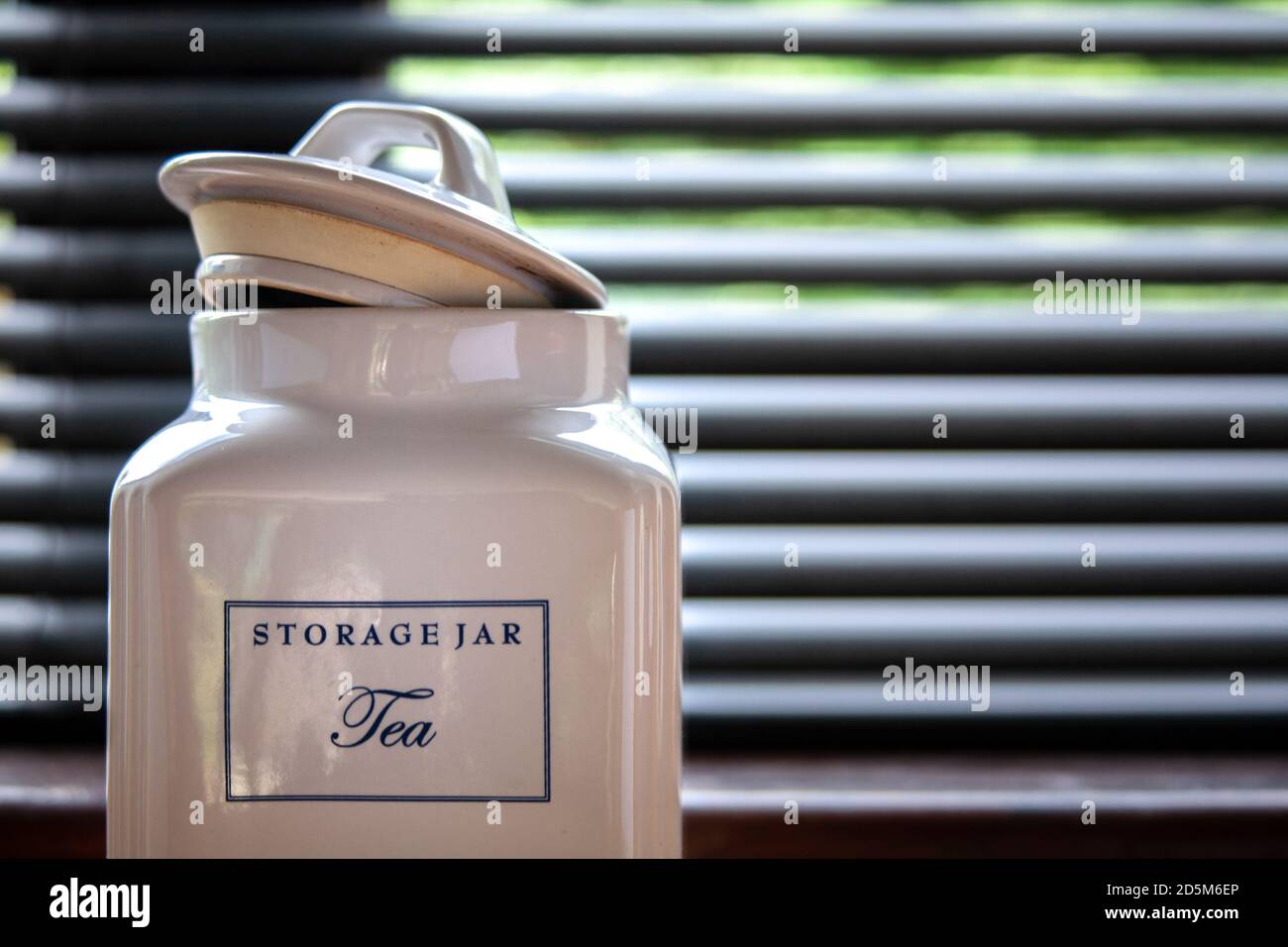 Ceramic tea storage pot with lid slightly ajar in kitchen. Window and ...