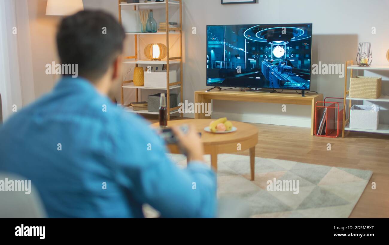 In the Living Room Man Sitting on a Couch Holds Controller Playing in a ...