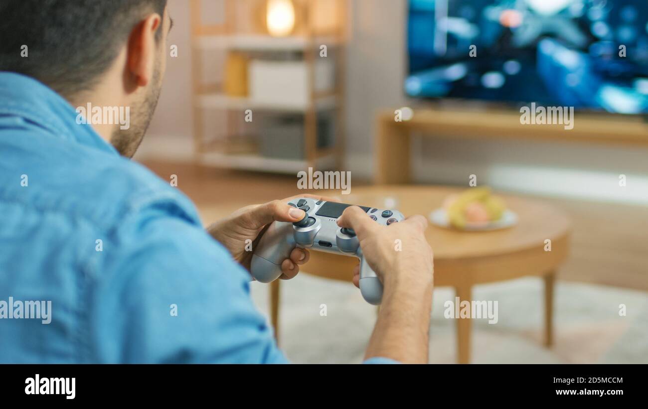In the Living Room Man Sitting on a Couch Holds Controller Playing in a ...