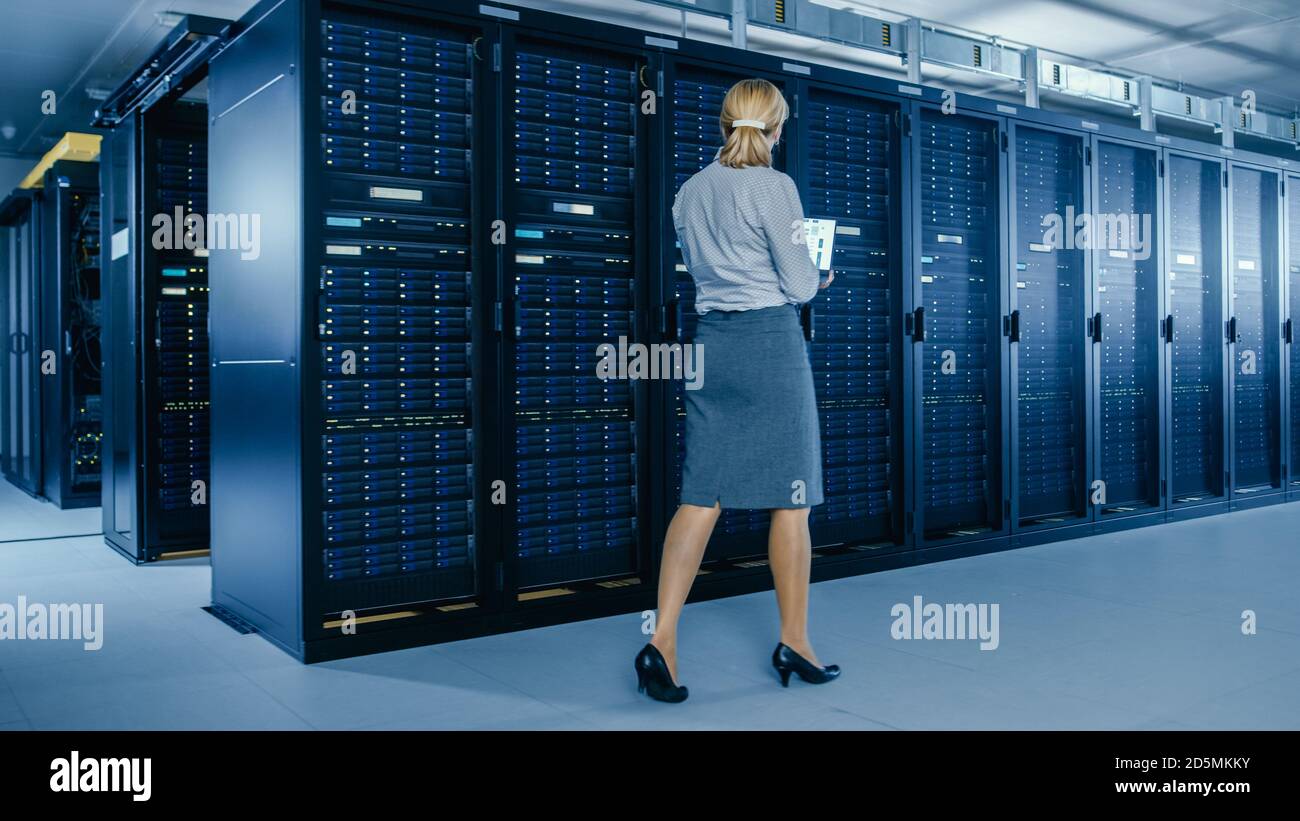 In Data Center: Female IT Specialist Walks along the Row of Operational ...