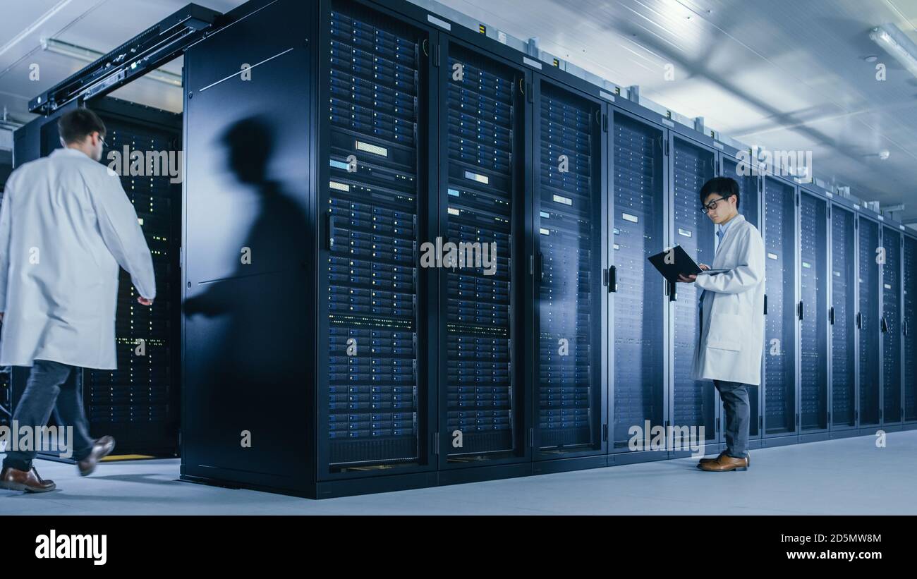 In Data Center: Male IT Technician Wearing White Coat Stands Beside ...