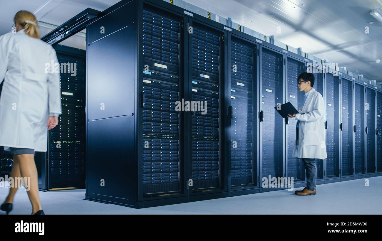 In Data Center: Male IT Technician Wearing White Coat Stands Beside ...