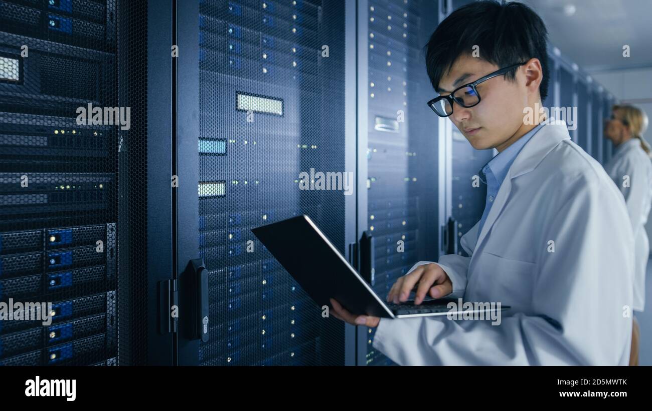 In Data Center: Male and Female IT Specialists Wearing White Coats Work ...