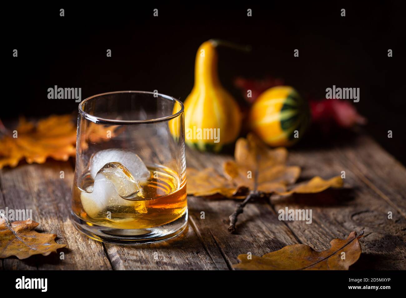 Glass of scotch whiskey and ice on wooden background with autumn leaves ...