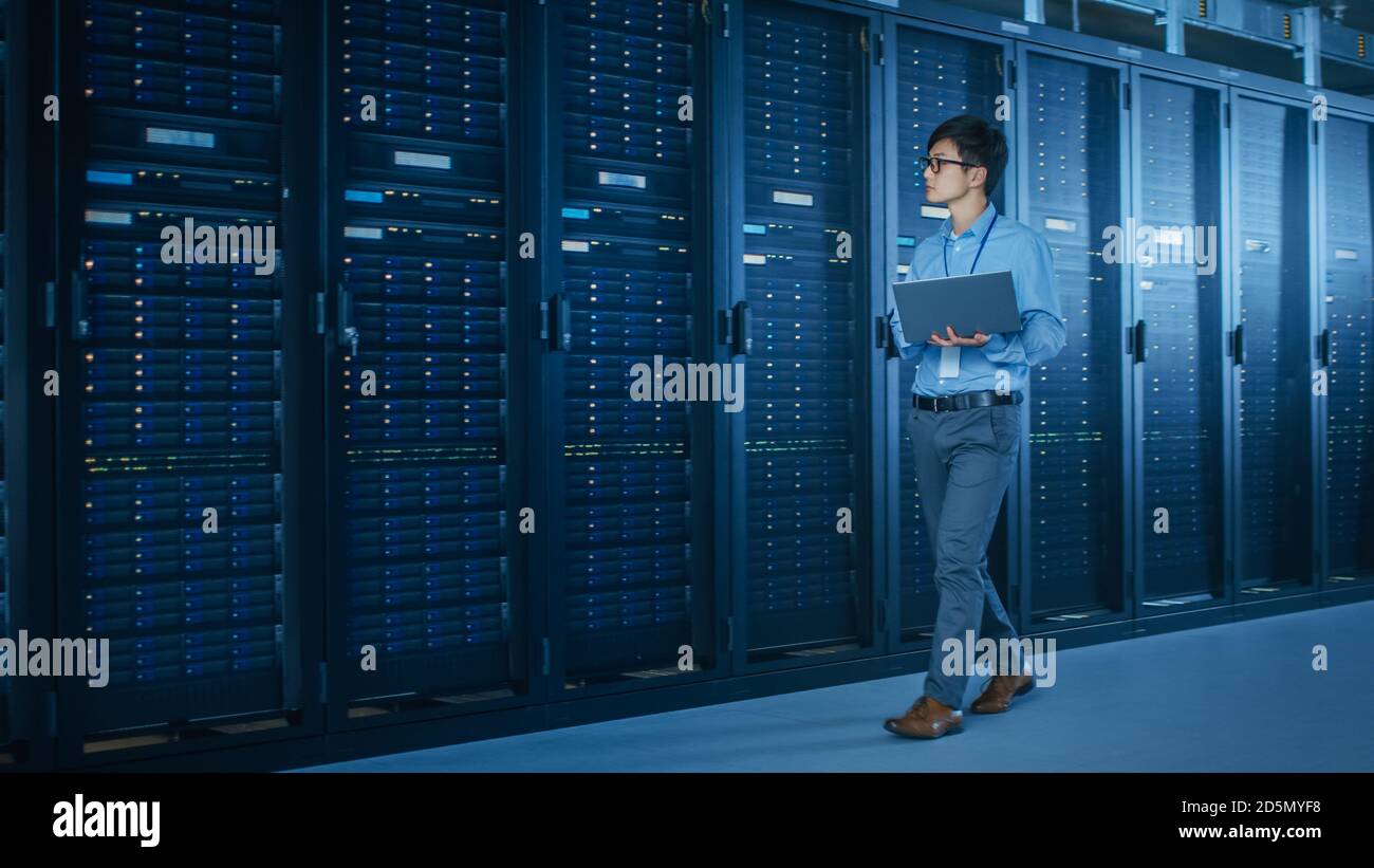 In the Modern Data Center: IT Engineer Working with Server Racks, Uses Laptop for Maintenance ...