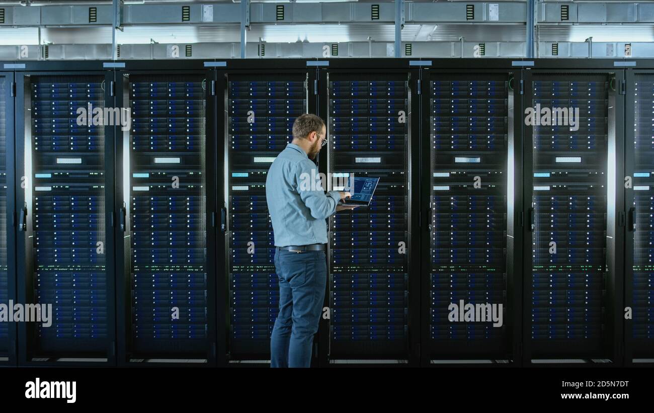 Bearded IT Specialist in Glasses is Working on Laptop in Data Center ...