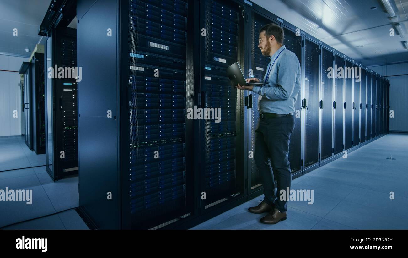 Bearded It Specialist In Glasses Is Working On Laptop In Data Center