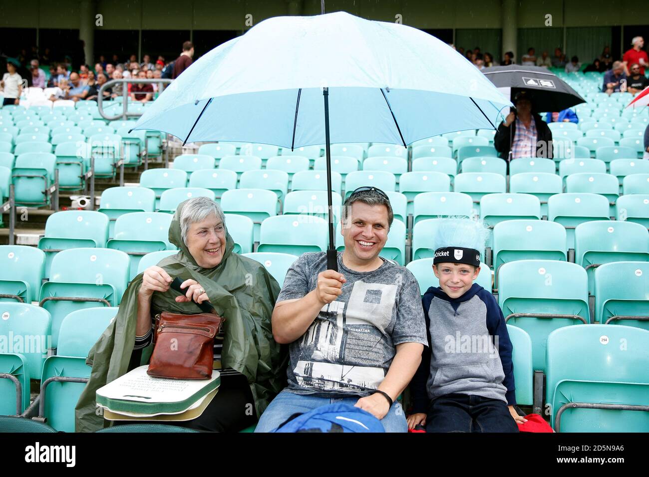 Surrey fans shield from the rain in the stands at the Kia Oval Stock ...