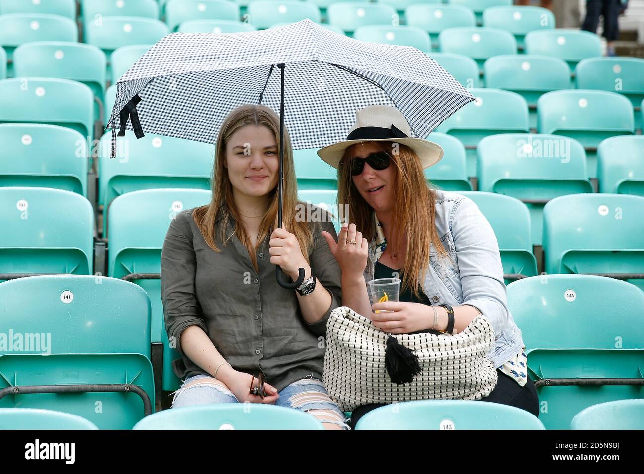 Surrey fans shield from the rain in the stands at the Kia Oval Stock ...