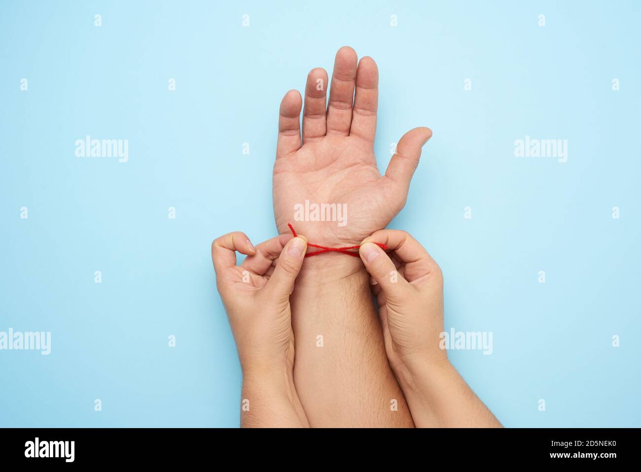 two female hands tie a red woolen thread on the wrist of a male hand ...