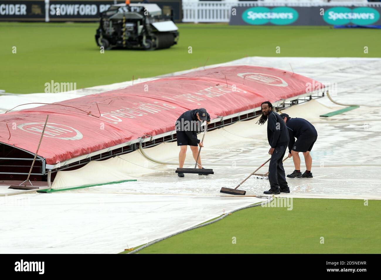 Ground staff sweep water off the covers during a rain delay in the ...
