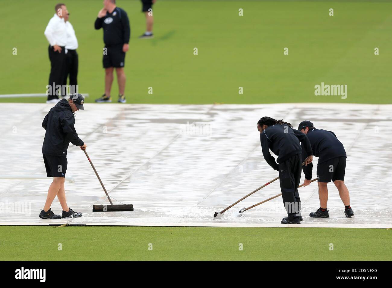 Ground staff sweep water off the covers during a rain delay in the ...