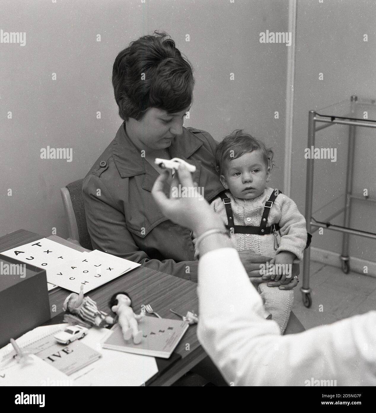 1970s, historical, a mother with her infant child seeing a doctor at a ...