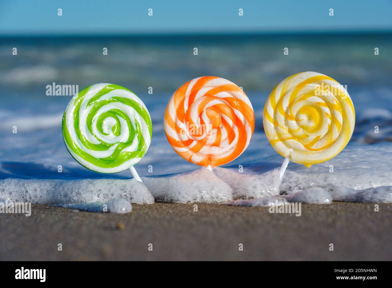 Closeup of three different lollipops on a beach surrounded by the sea ...