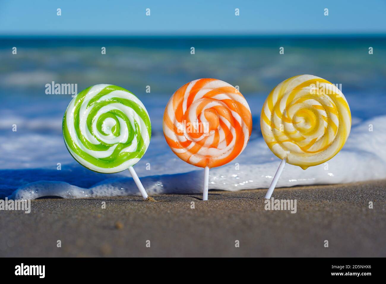 Closeup of three different lollipops on a beach surrounded by the sea ...