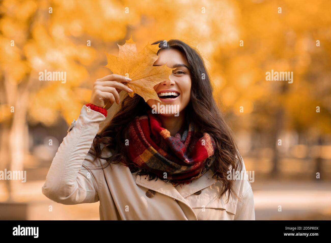 Lovely millennial woman smiling and closing her eye with yellow autumn ...