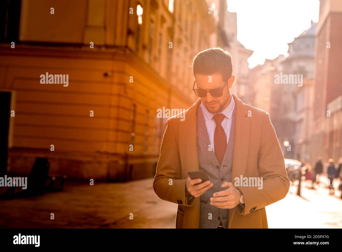 A handsome elegant man walking on the streets and using his smartphone ...