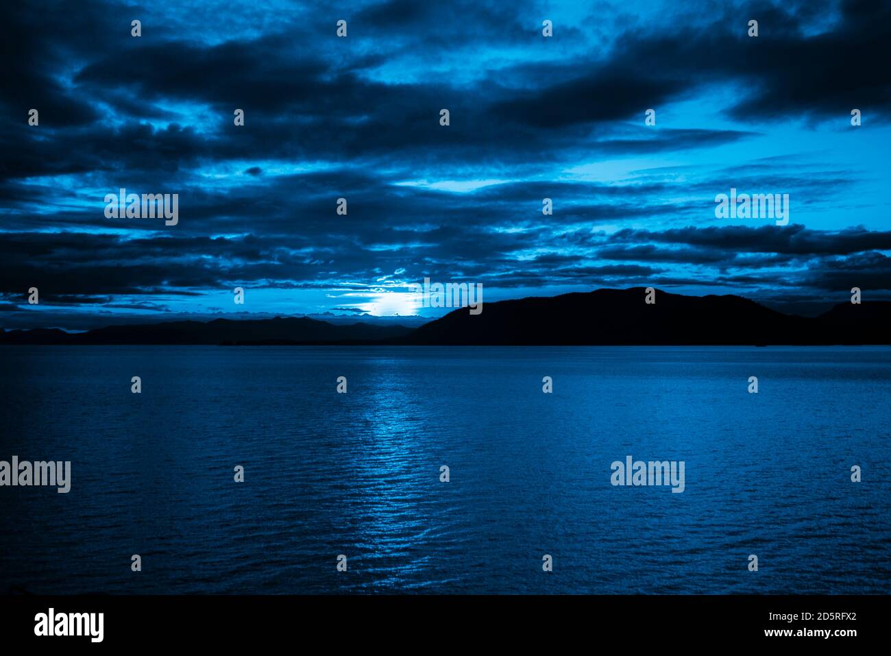 Sun setting over the Alaskan coastline during summer, with a blue ...