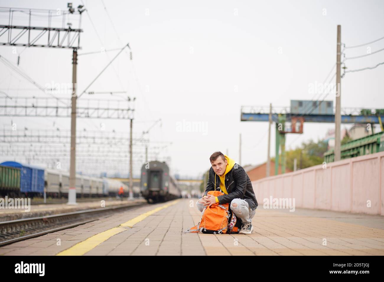 Young man squats on platform, waiting for train. Male passenger with ...