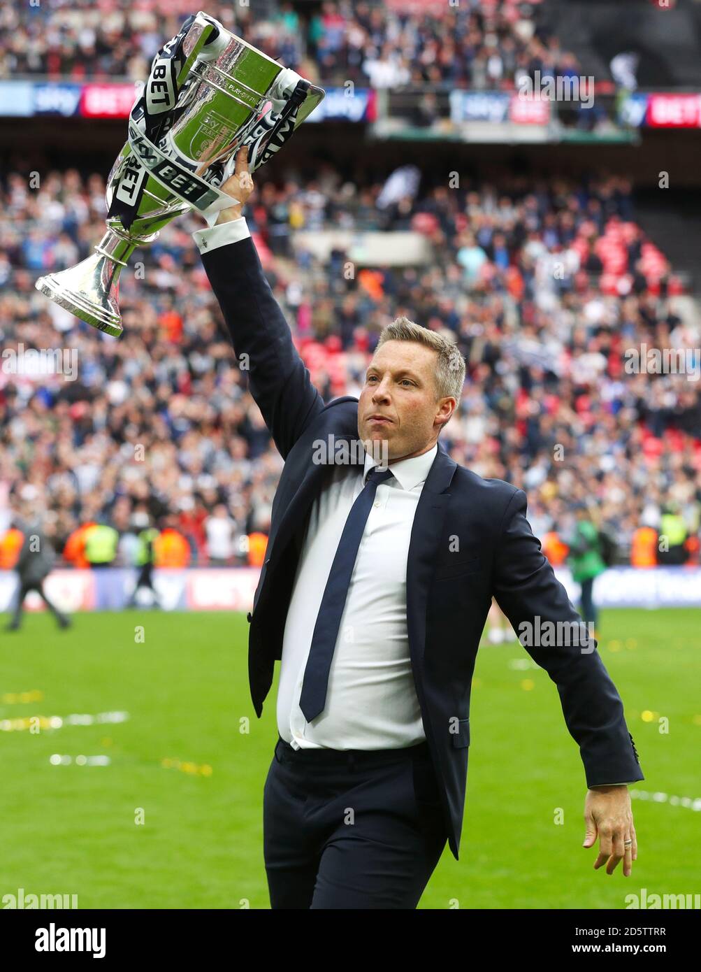Millwall manager Neil Harris celebrates with the trophy on the pitch ...