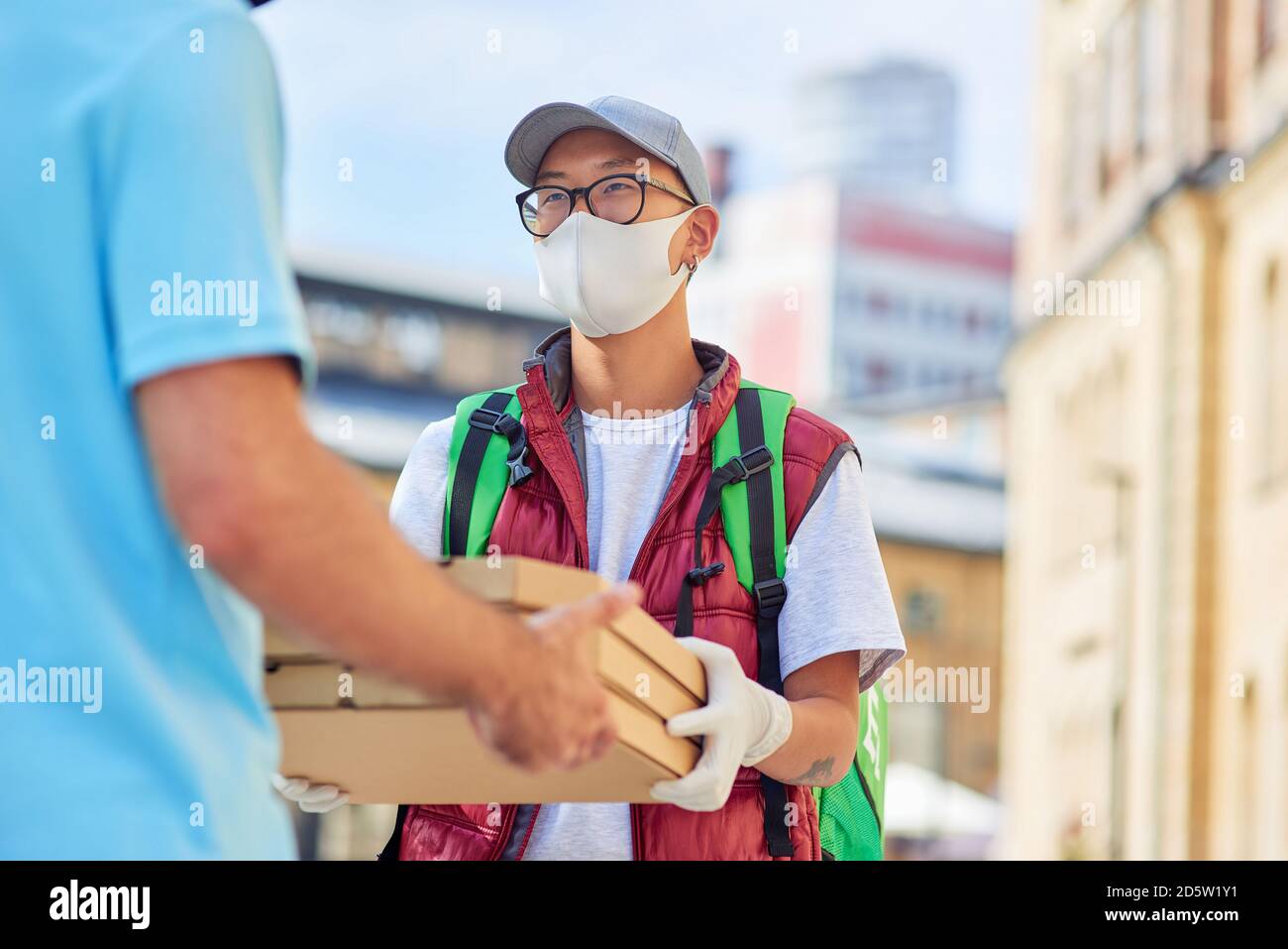 Young friendly asian delivery man in protective mask and gloves giving ...