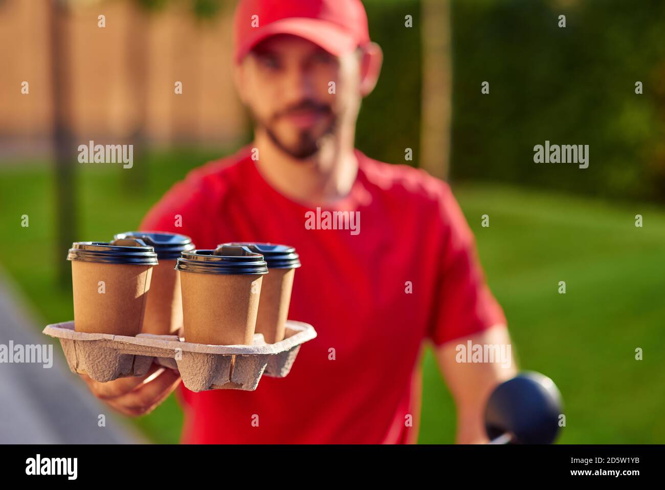 Coffee cups standing on delivering board in hand of man courier ...