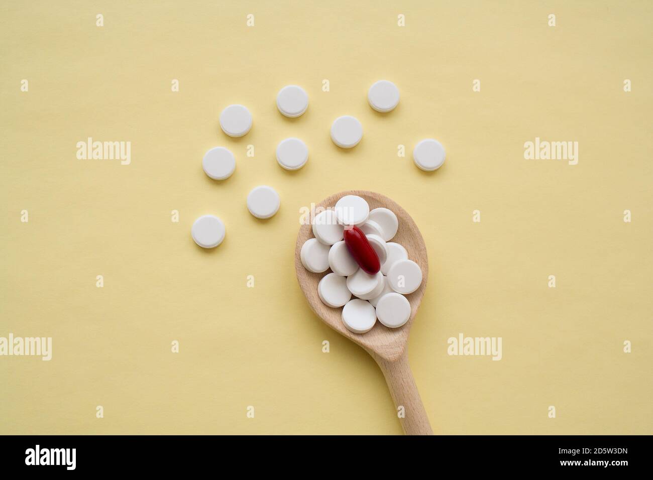 round white tablets with one red capsule on a wooden spoon on a yellow ...