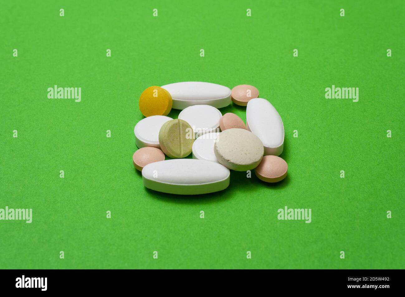 Bunch colorful round pills and capsules on a green background close up ...