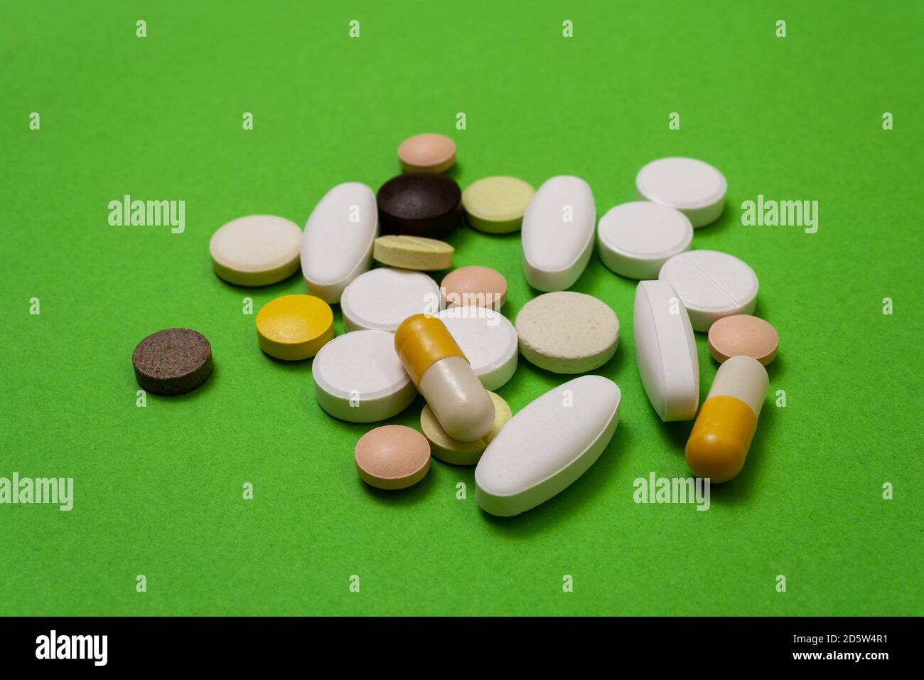 Many colorful round pills and capsules on a green background close up ...