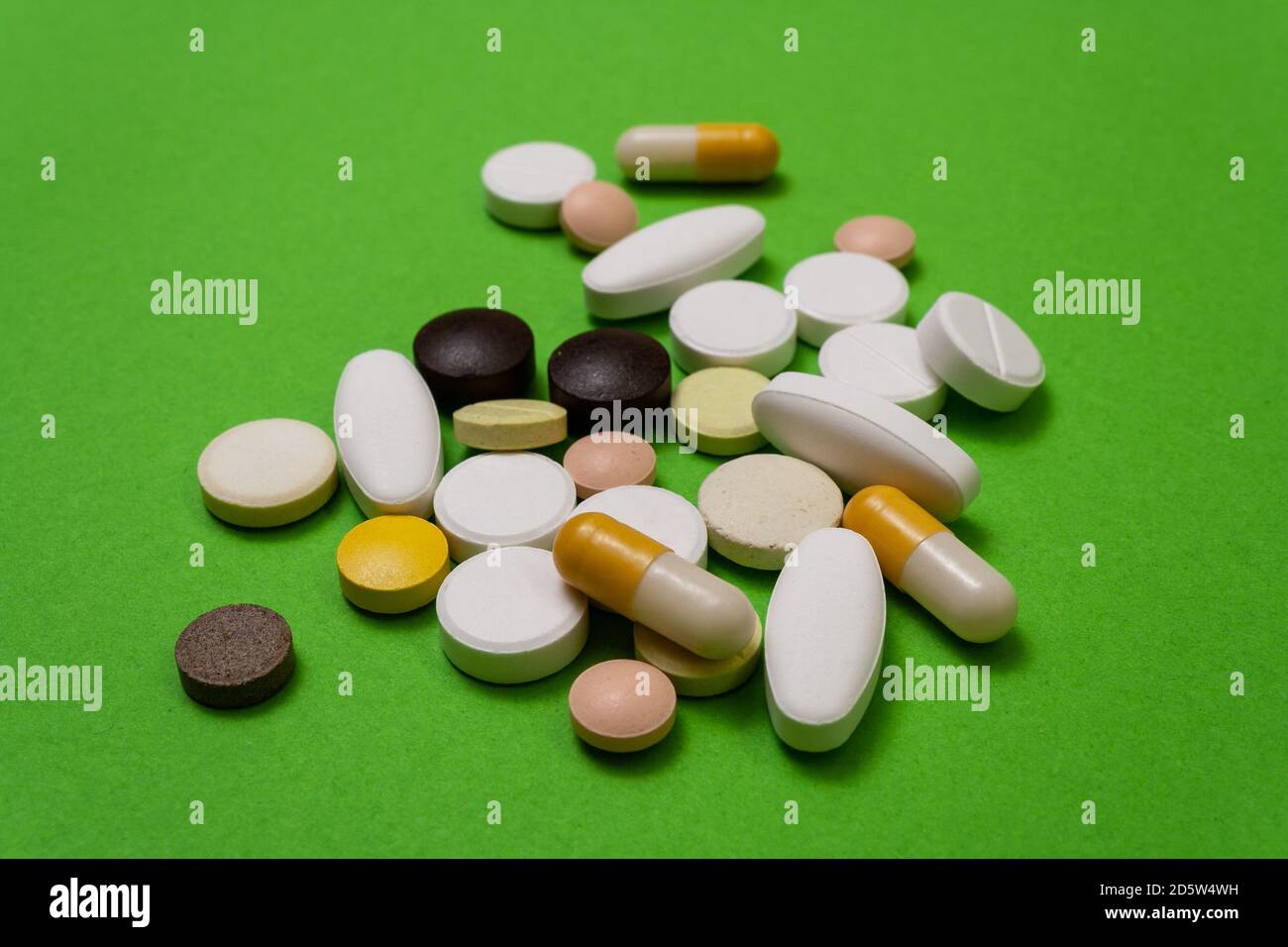 Many colorful round pills and capsules on green background of table ...