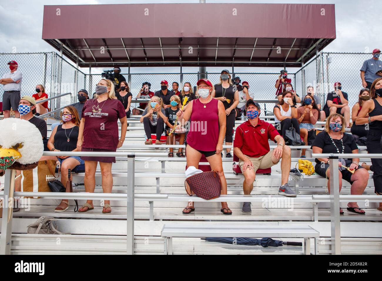 A group of masked spectators cheer on a football team from bleachers ...