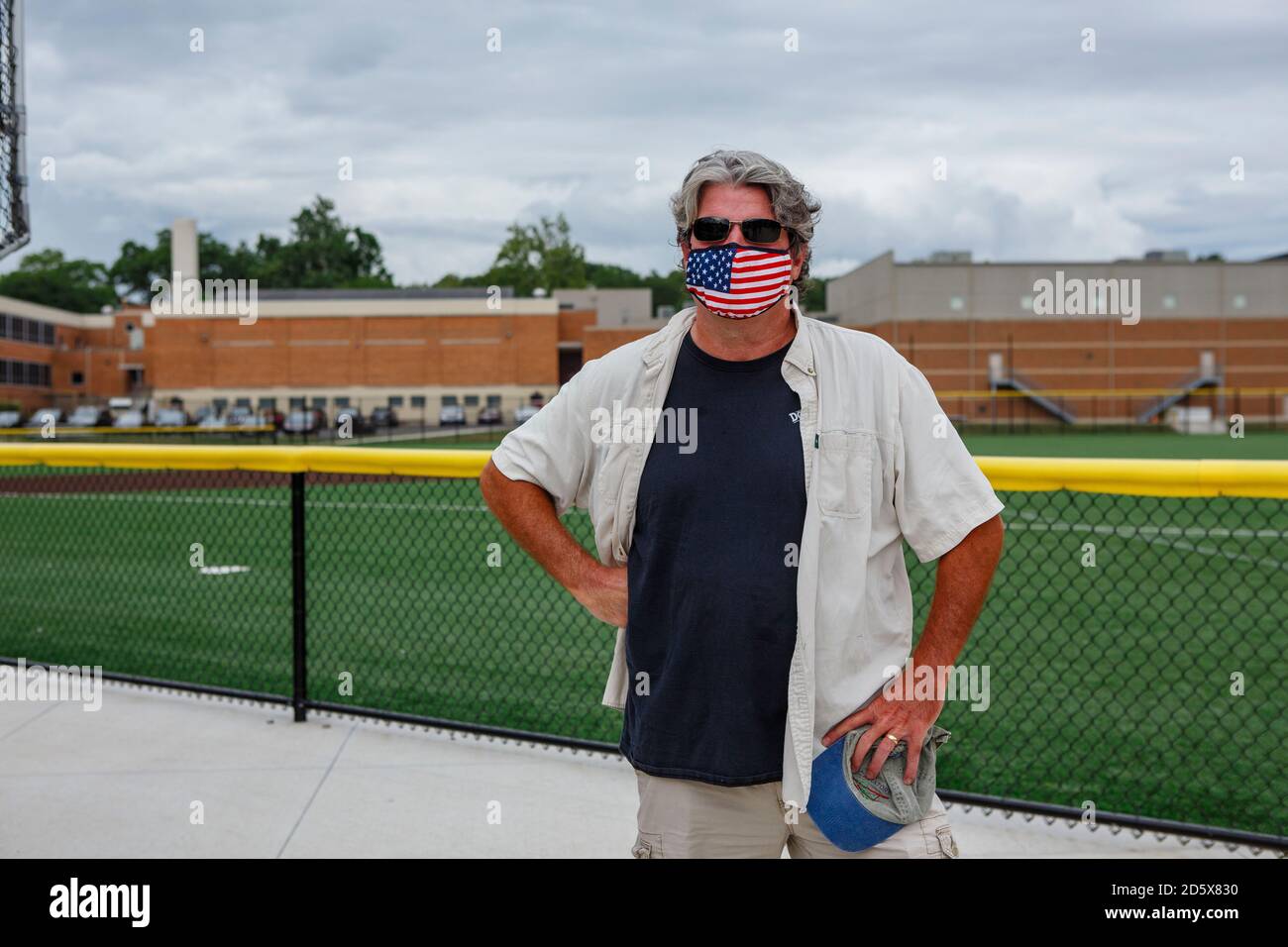 An older man stands in front of chain link fence wearing a flag mask ...