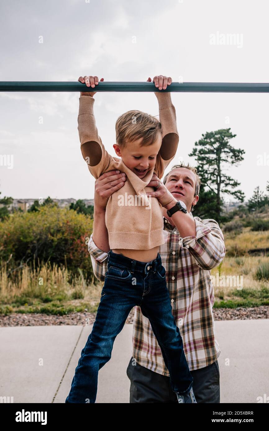Dad helping young son up on to a bar at a playground Stock Photo - Alamy