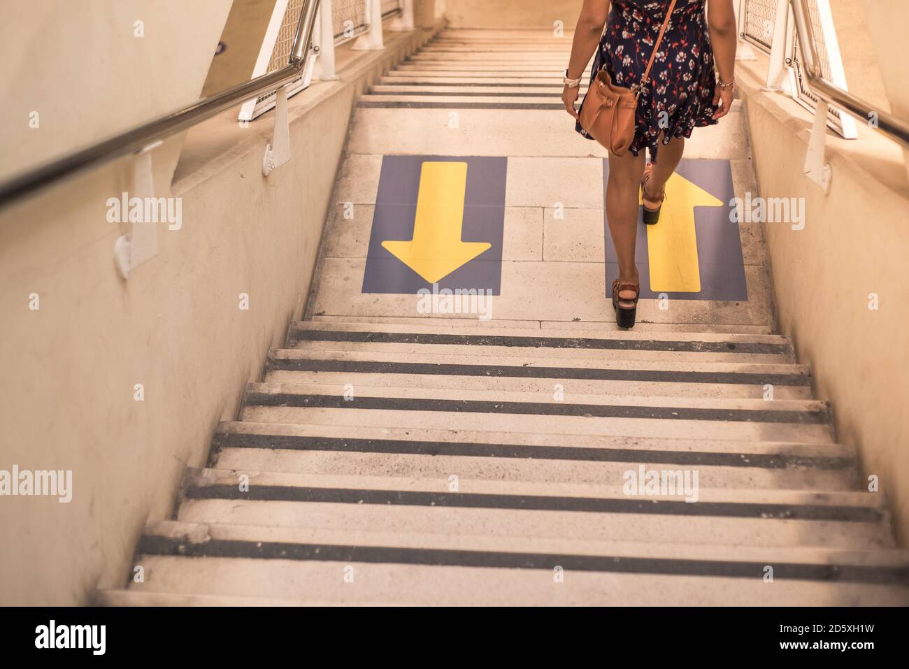 Young woman wearing a dress going down the stairs with floor arrows on ...