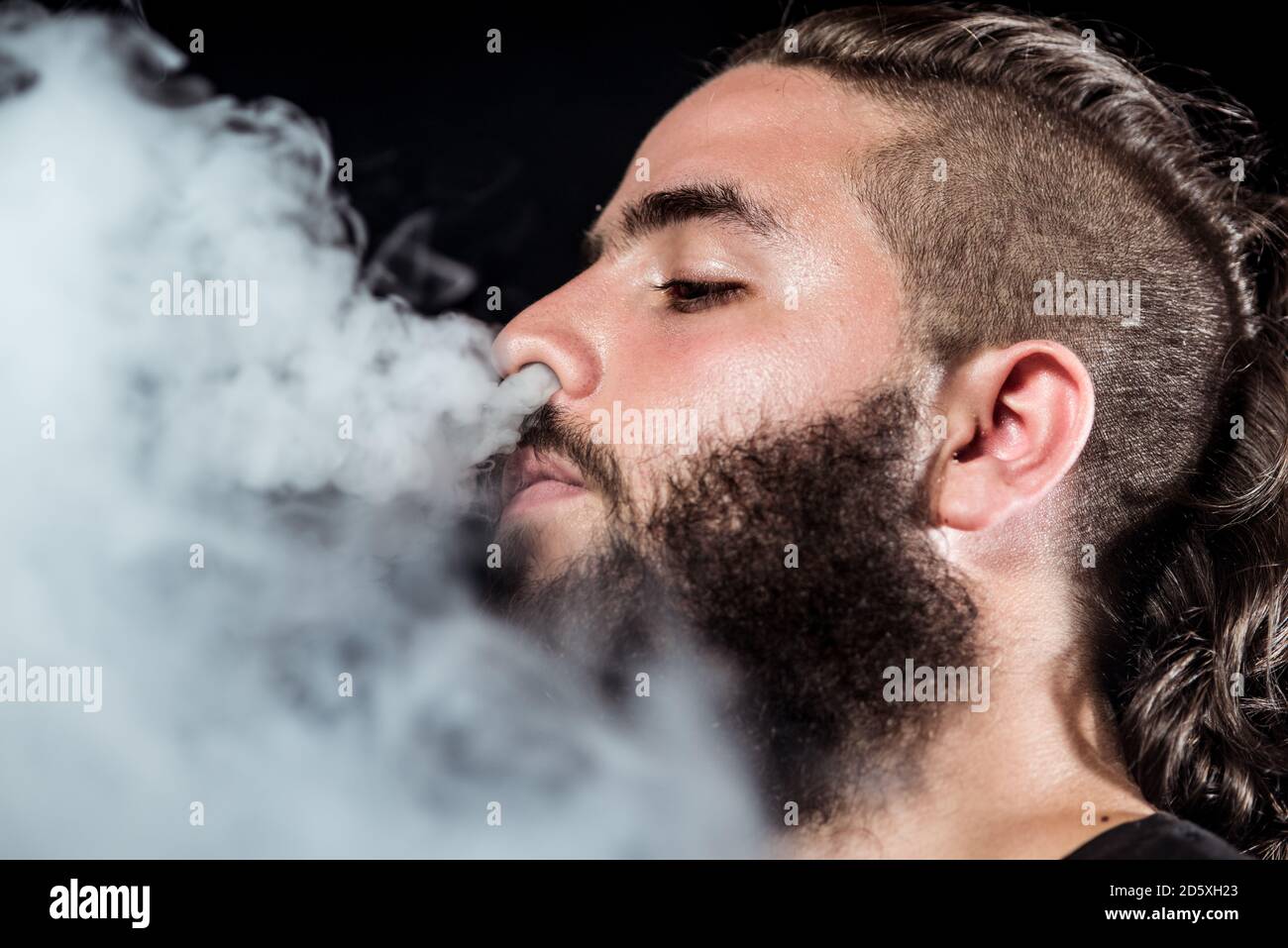 Close up face young man throw smoke through the nose with a long beard ...