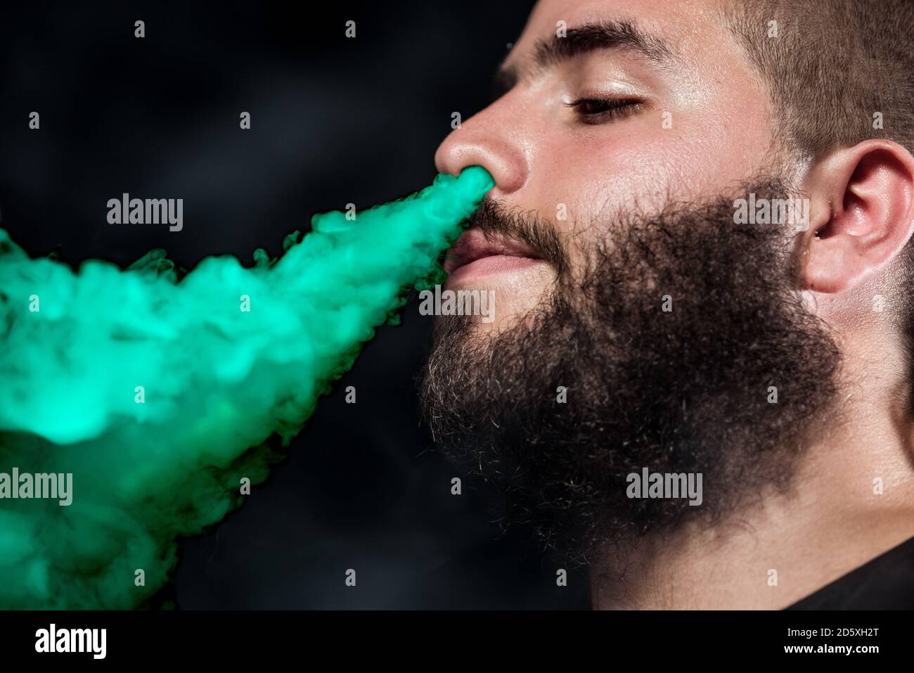 Young caucasian man pull green smoke through the nose with a long beard ...