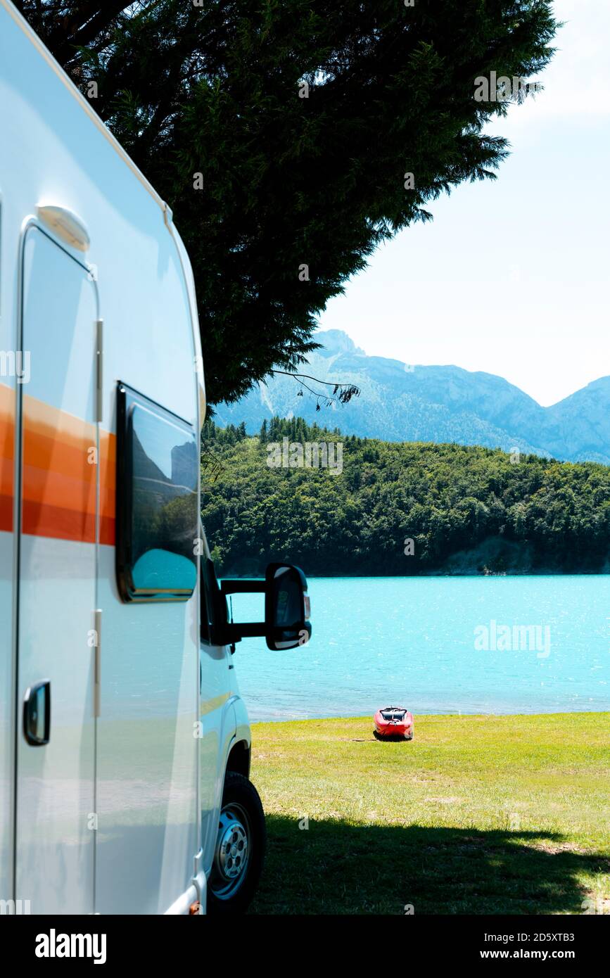 RV motorhome in front of a blue lake with mountains and a red Kayak ...