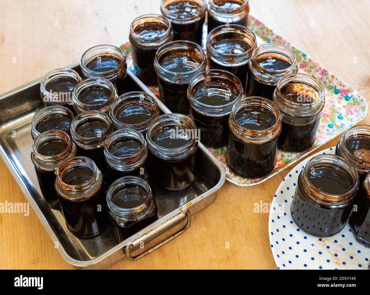 Open topped jam jars filled with setting dark liquid quince jam jelly ...