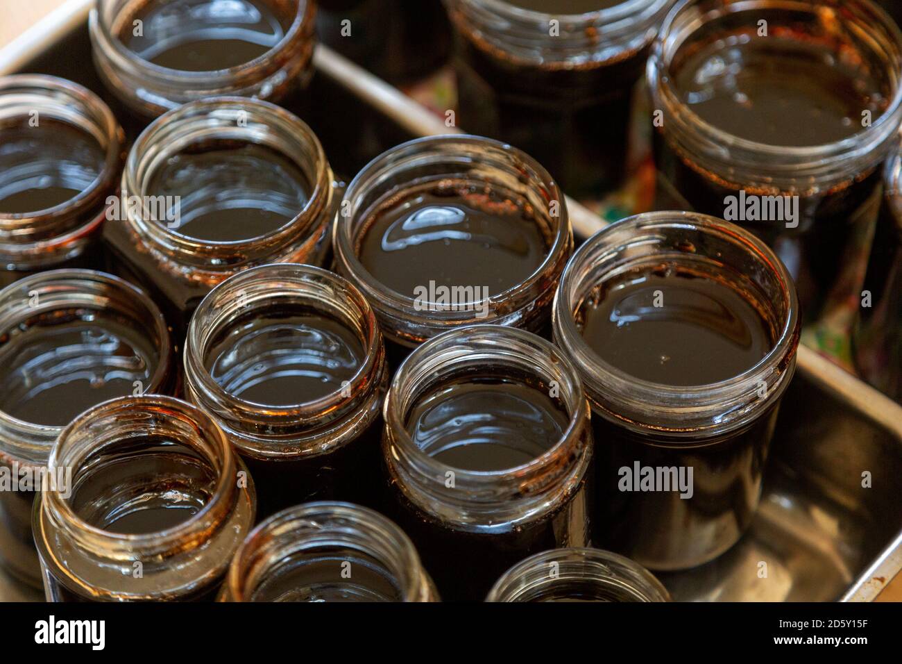 Open topped jam jars filled with setting dark liquid quince jam jelly ...