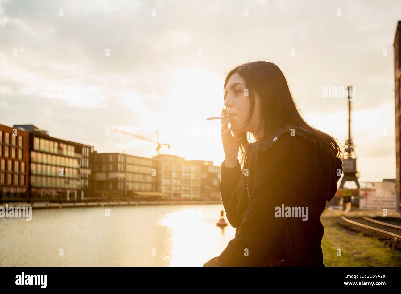 Germany, Muenster, young woman smoking cigarette in front of city ...