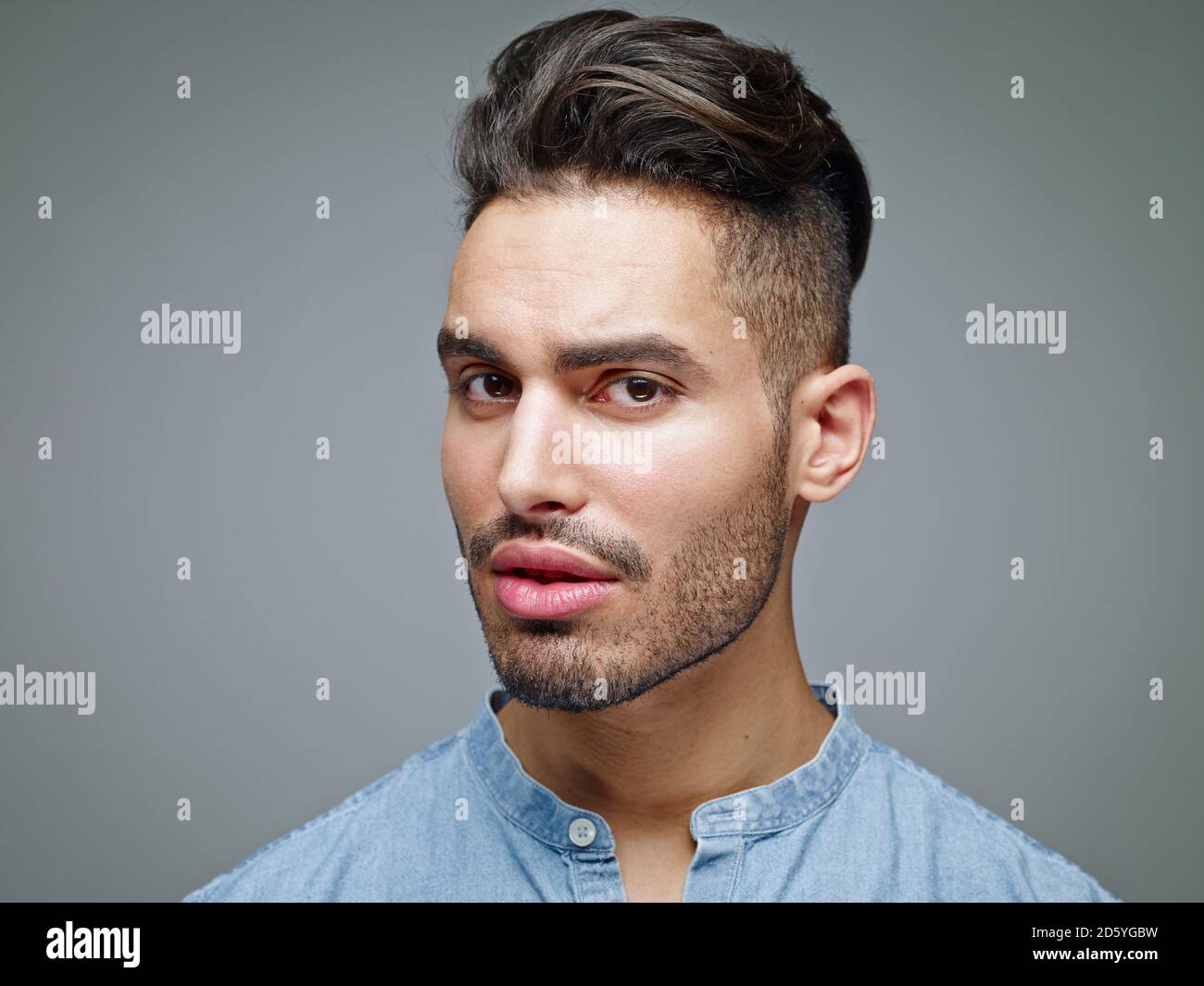 Portrait of sceptical looking young man in front of grey background ...