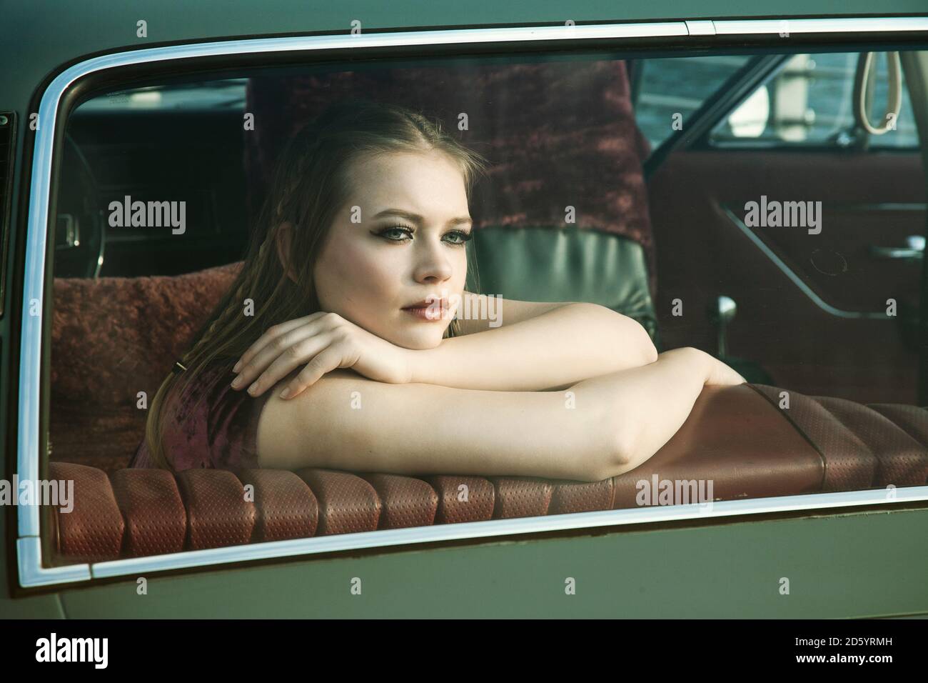 Portrait of young woman looking through rear window of vintage car ...